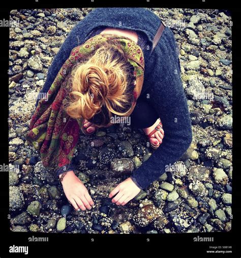 Girl On Rock Beach Bending Over Picking Up Crabs And Stones With Her