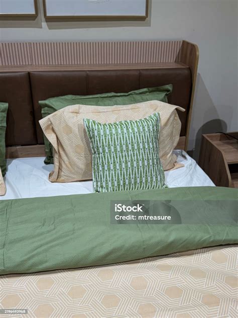 패딩 처리된 더블 침대 가죽 커버 헤드보드 일체형 목재 선반 갈색과 초록색 코디형 침구 베개 및 쿠션 스택 흰색 침대 시트 접힌 이불 전경에 초점 높은 전망 부드러운 가정용