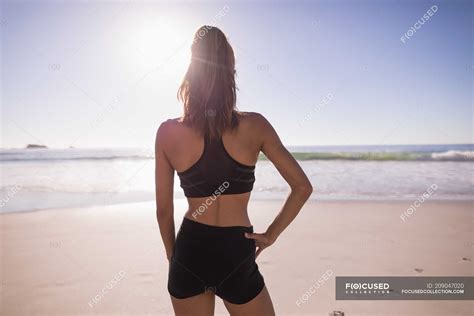 Fit Woman Standing With Hand On Hip In Beach At Dusk Rear View