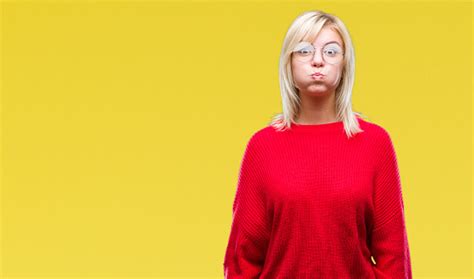 젊은 아름 다운 금발 여자 재미 있은 얼굴 뺨 피 격리 된 배경 위에 스웨터와 안경 착용 입 어 미친 식으로 팽창 가득 찬에