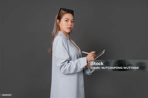 아시아의 장발 여성 임원 또는 회사 직원 파란색 양복과 세련된 안경을 쓰고 펜과 태블릿을 사용하여 보고 작업합니다 회색 배경