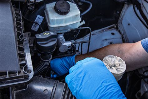 파란 장갑을 낀 자동차 정비사 더러운 자동차 냉각수 저장 탱크 필터를 들고 열린 차량 후드 근처에서 유지 보수 및 수리를 위해 엔진 부품을 검사합니다 차량 냉각 시스템 고정