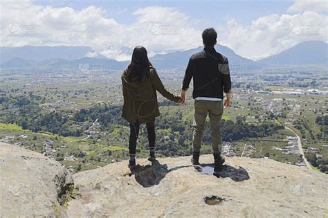 在危地马拉的quetzaltenango，一对年轻夫妇手牵着手站在山顶享受自然——年轻人在悬崖边看着