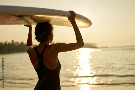 African American Woman Standing With Surfboard On Her Head On Ocean