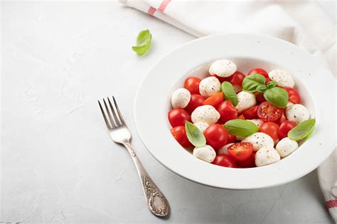 잘 익은 토마토 모 짜 렐 라와 신선한 바 질 맛 있는 클래식 Caprese 샐러드의 흰색 접시 회색 배경 복사 공간에 나뭇잎 이탈리아 음식입니다 건강 한 채식의 개념 0