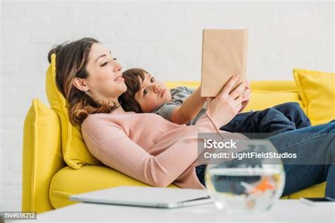 함께 소파에 누워 있는 동안 귀여운 소년 독서 책과 예쁜 웃는 여자 2명에 대한 스톡 사진 및 기타 이미지 2명 가정 생활