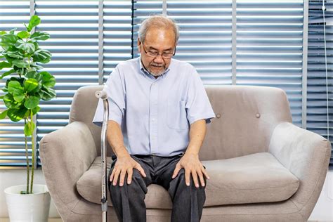 Pensive Senior Man Leaning On Walking Stick While Sitting On Sofa