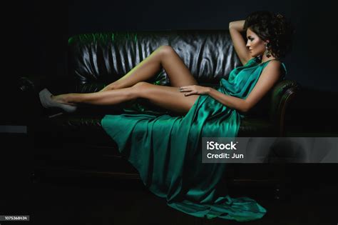 Woman Wearing Beautiful Green Silk Dress Is Posing On Leather Couch
