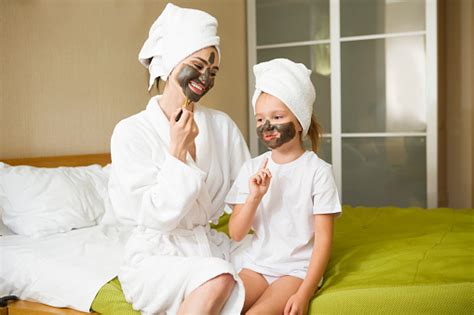엄마와 딸은 집에서 점토 얼굴 마스크를 만들고 있습니다 그들의 머리는 흰색 목욕 수건으로 싸여 있습니다 함께 쾌활한 시간
