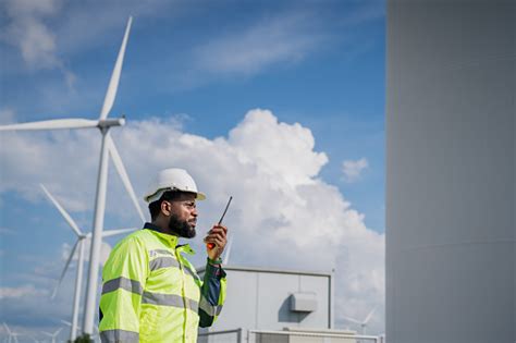 노란색과 검은색 안전조끼를 입은 남자가 풍력 터빈 옆에 서 있습니다 그는 무전기를 들고 있습니다 전기 엔지니어 환경 에너지 깨끗한 지속 가능 풍력 터빈 자연 40 44세에