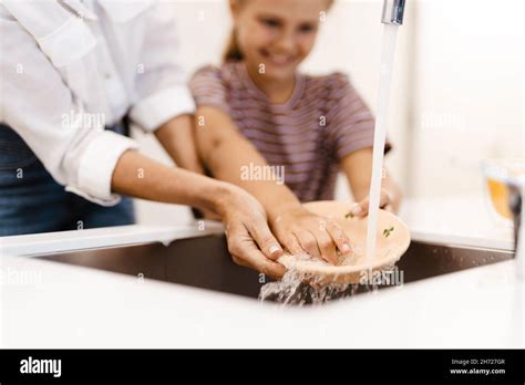White Mother And Daughter Smiling While Washing Dishes Together In