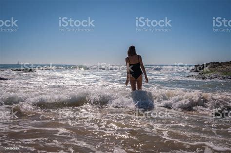 검은 색 수영복을 입은 짧은 머리를 가진 젊은 여성이 바다의 성난 요소로 걸어갑니다 러시아에 대한 스톡 사진 및 기타 이미지