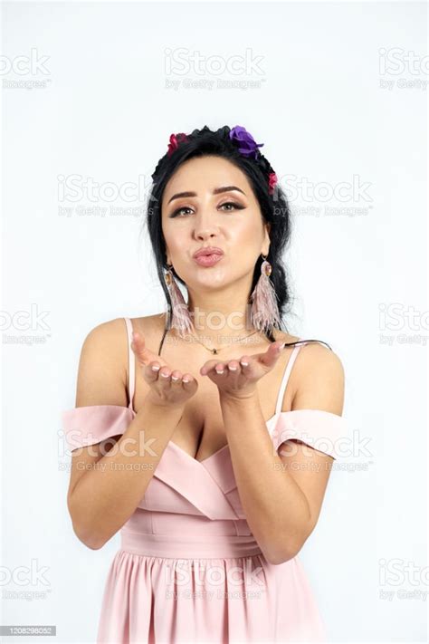 세련된 젊은 갈색 머리 소녀 또는 모델은 키스를 불고 그녀의 머리에 꽃후프와 세련된 핑크 드레스를 입고 흰색 배경에 스튜디오 촬영 갈색 머리에 대한 스톡 사진 및 기타