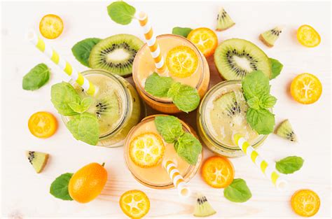 갓 혼합된 오렌지 금 귤과 짚 민트 잎으로 유리 항아리에 그린 키 위 과일 스무디 익은 베리 평면도 닫습니다 화이트 나무 보드