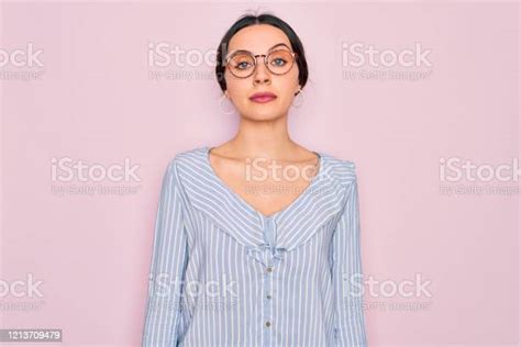 젊은 아름 다운 여자 캐주얼 스트라이프 셔츠와 안경을 입고 분홍색 배경 에 얼굴에 심각한 표정으로 편안 하 게 카메라를 보는 간단하고 자연스러운 눈 신체 부분에 대한 스톡