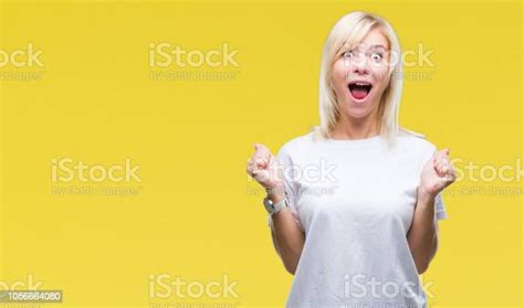 축 하 하는 고립 된 배경 위에 흰색 T셔츠를 입고 젊은 아름 다운 금발의 여 자가 놀라게 하 고 무기와 성공을 위한 제기 및