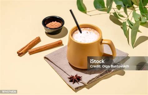 거품이 많은 커피 라떼 핫 초콜릿 또는 코코아와 함께 노란색 컵 계피 스틱 아니스 별 노란색 배경 단단한 그림자와 녹색 가지 0