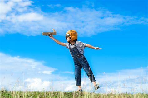 화창한 날에 장난감 비행기를 손에 들고 초원을 뛰어 다니는 귀여운 소녀 푸른 여름 하늘 배경에 골판지 비행기로 노는 행복한 아이 어린 시절의 꿈 상상력 개념 비행기에 대한