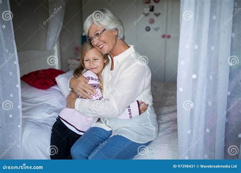 Smiling Grandmother And Granddaughter Embracing Each Other On Bed Stock