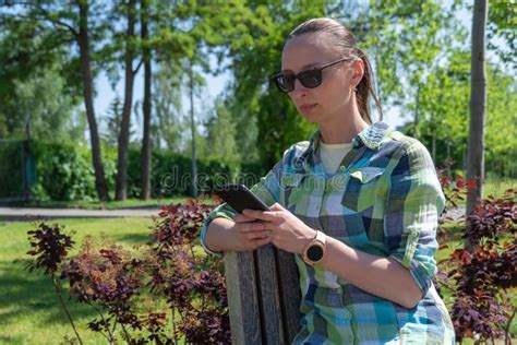 Woman Sitting On Park Bench And Flip Through Display On Mobile Phone