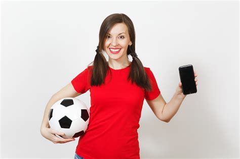 유럽 젊은 여자 두 조랑말 꼬리 축구 팬 이나 선수 붉은 유니폼 보류 축구공 흰색 배경에 고립 된 휴대 전화에에서 재미 스포츠