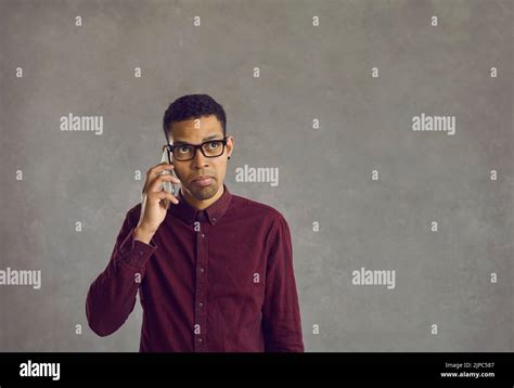 Confused Young Black Man Holding Mobile Phone Making Call And Waiting