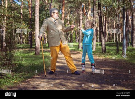 Grandfather Walks With His Granddaughter In The Park A Girl Roller