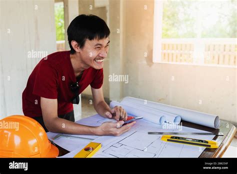 Engineer Or Architect Using Cell Phone On Blueprint In Building Construction Site Stock Photo