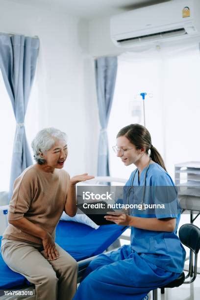 친절한 여성 간호사가 침대에서 쉬고 있는 환자를 검진합니다 그녀는 병원에서 성공적인 수술 후 완전히 회복하는 동안 태블릿을