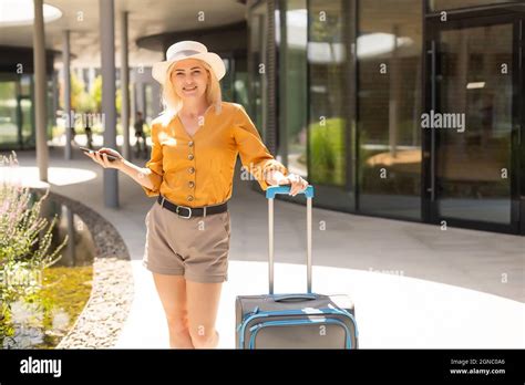 Businesswoman Pulling Her Suitcase And Checking Her Phone Stock Photo