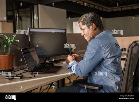 black man writing lines of code on desktop pc with two monitors and a