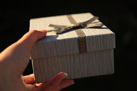 최소한의 검은 색 배경에 리본 리본으로 감싸인 빈티지 선물 상자를 들고 있는 여성 핸드 상자를 제시합니다 휴일 개념 축제 배경