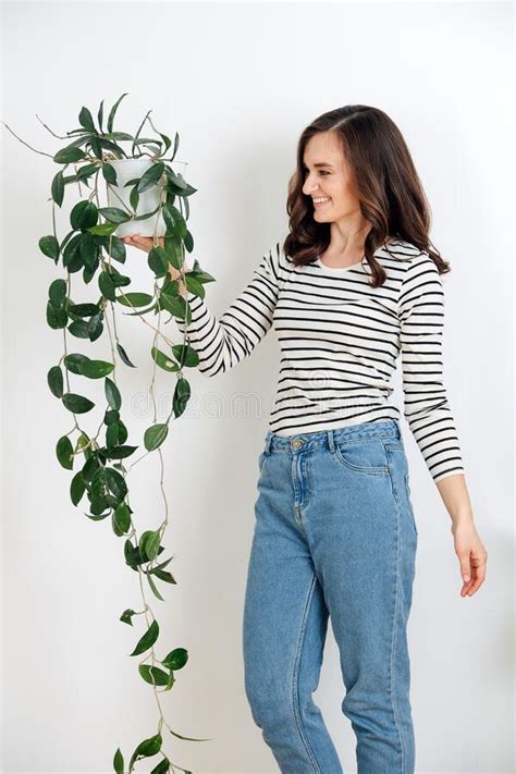 Happy Brunette Woman Holding A Potted Plant In Her Hand Looking At It