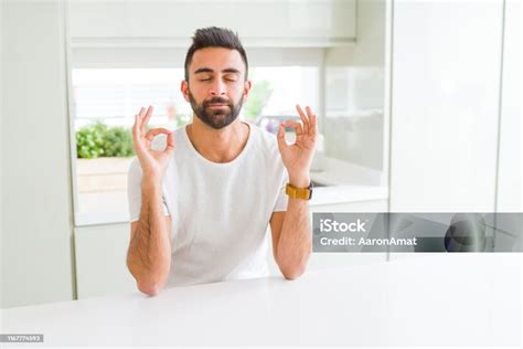 잘 생긴 히스패닉 남자 캐주얼 흰색 티셔츠 집에서 휴식과 손가락으로 명상 제스처를하고 눈을 감고 미소 요가 개념입니다 T 셔츠에 대한 스톡 사진 및 기타 이미지 Istock