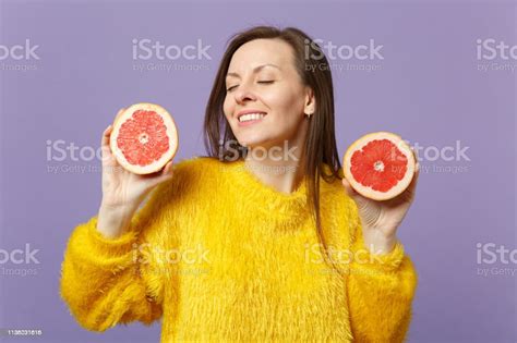 모피 스웨터에 예쁜 젊은 여 자가 보라색 파스텔 배경에 고립 된 신선한 잘 익은 자 몽의 Halfs 지주를 유지 사람들은 생생한