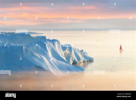 Little Red Sailboat Cruising Among Floating Icebergs In Disko Bay