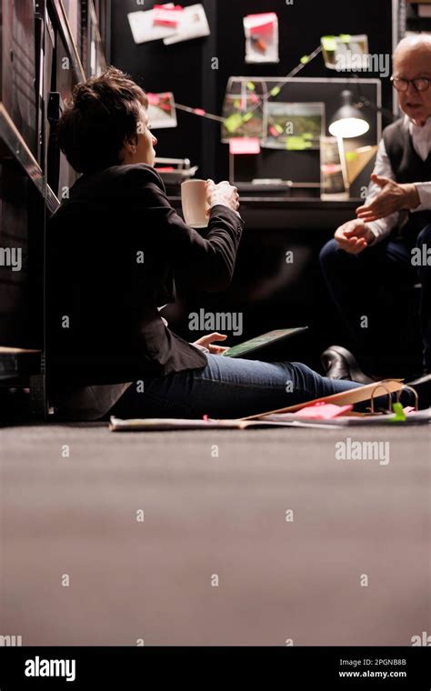 Tired Police Officer Analyzing Victim Report In Arhive Room Discussing Crime Scene Evidence