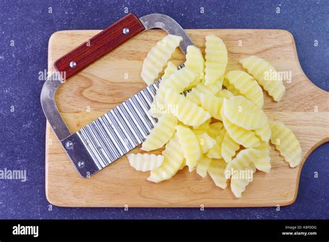 Potato Peeled And Cut In Pieces With A Special Knife With Ribs On A Cutting Board On A Grey