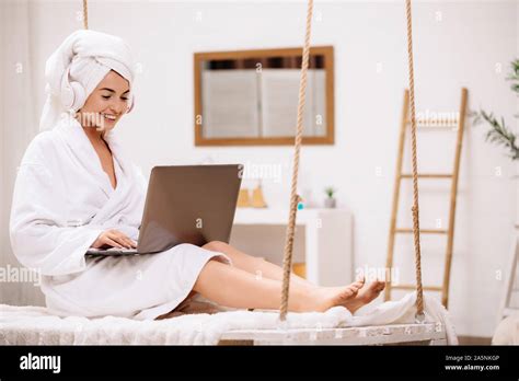 Woman In Bathrobe And Towel After Shower Uses Laptop In Bedroom Stock