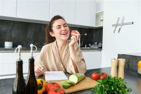 Portrait Of Happy Brunette Woman Bites Tomato Sits In The Kitchen