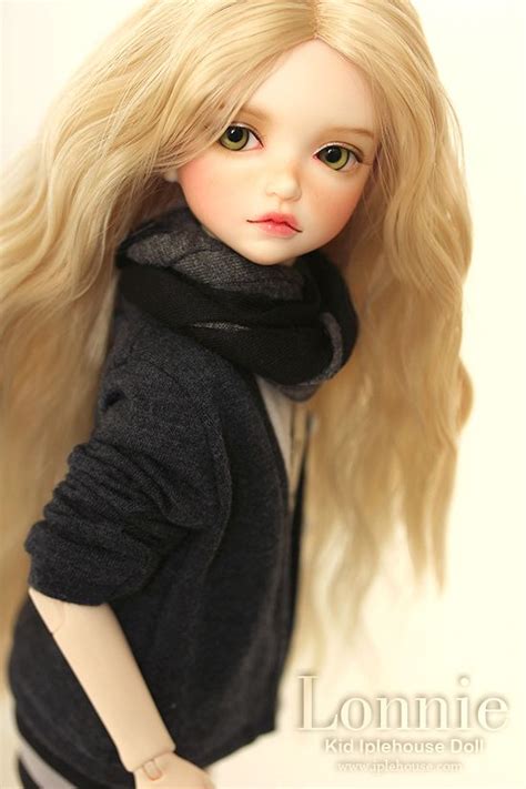 A Doll With Long Blonde Hair Wearing A Black Sweater And Gray Scarf