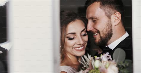 화려한 신부와 세련된 신랑이 창가에서 부드럽게 포옹하고 있다 행복한 결혼식 커플은 포옹하고 웃고 있다 신혼 부부의 낭만적 인 순간 창조적 인 결혼식 사진입니다 복사