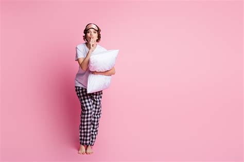 Shh 재미 있은 아가씨 홀드 베개 손가락 입술에 단어 착용 마스크 화이트 티셔츠 체크 무늬 파자마 바지 맨발 고립 된 핑크 색