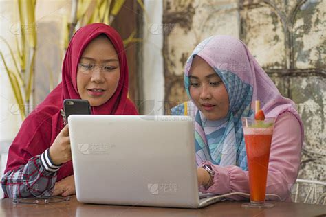 年轻、快乐、美丽的穆斯林女学生，戴着传统的伊斯兰头巾，在网上谈生意，用笔记本电脑在咖啡馆一起工作，以