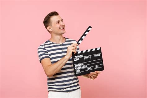 Clapperboard 동향 파스텔 핑크 배경에 절연을 만드는 고전적인 흑인 영화를 들고 줄무늬 티셔츠를 입고 젊은이의 초상화