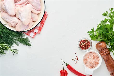 가벼운 슬레이트 돌 또는 콘크리트 배경에서 요리하기위한 향신료와 재료와 흰색 그릇에 원시 닭 날개 복사 공간이 있는 상단