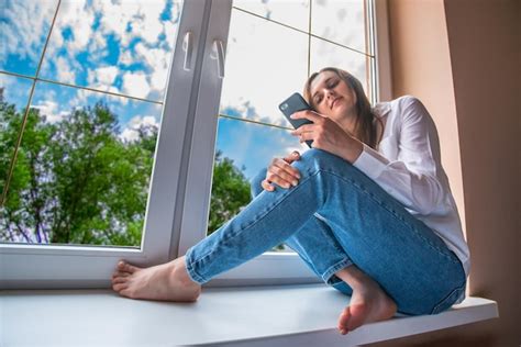 Premium Photo A Woman Sits On A Windowsill And Looks At Her Phone