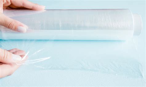 투명 한 폴 리 에틸렌 식품 필름 롤을 사용 하 여 파스텔 블루 테이블에 제품을 포장 하는 여자의 손 부엌에 대한 스톡 사진 및