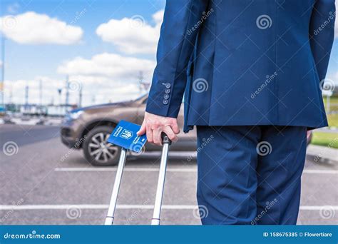 Мужчина в синем костюме с чемоданом и украинским паспортом на стоянке аэропорта на фоне его