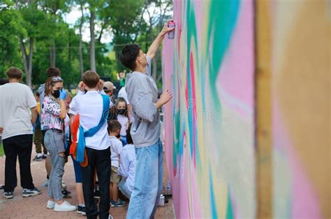 Young Asian Male Artist Creating Colorful Mural On Pink Wall In Public